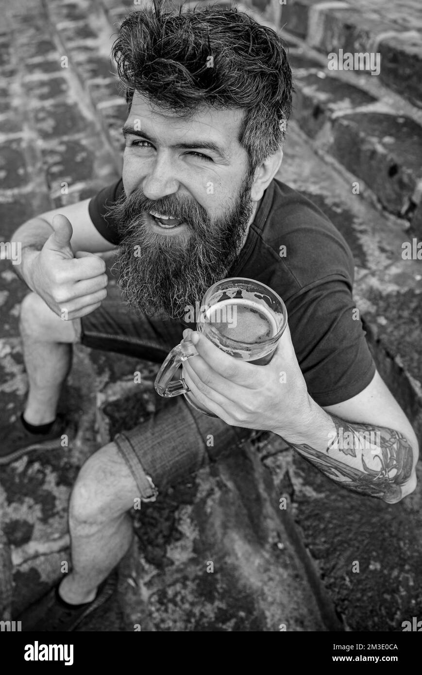 Man with beard and mustache holds glass with beer and shows thumb up ...