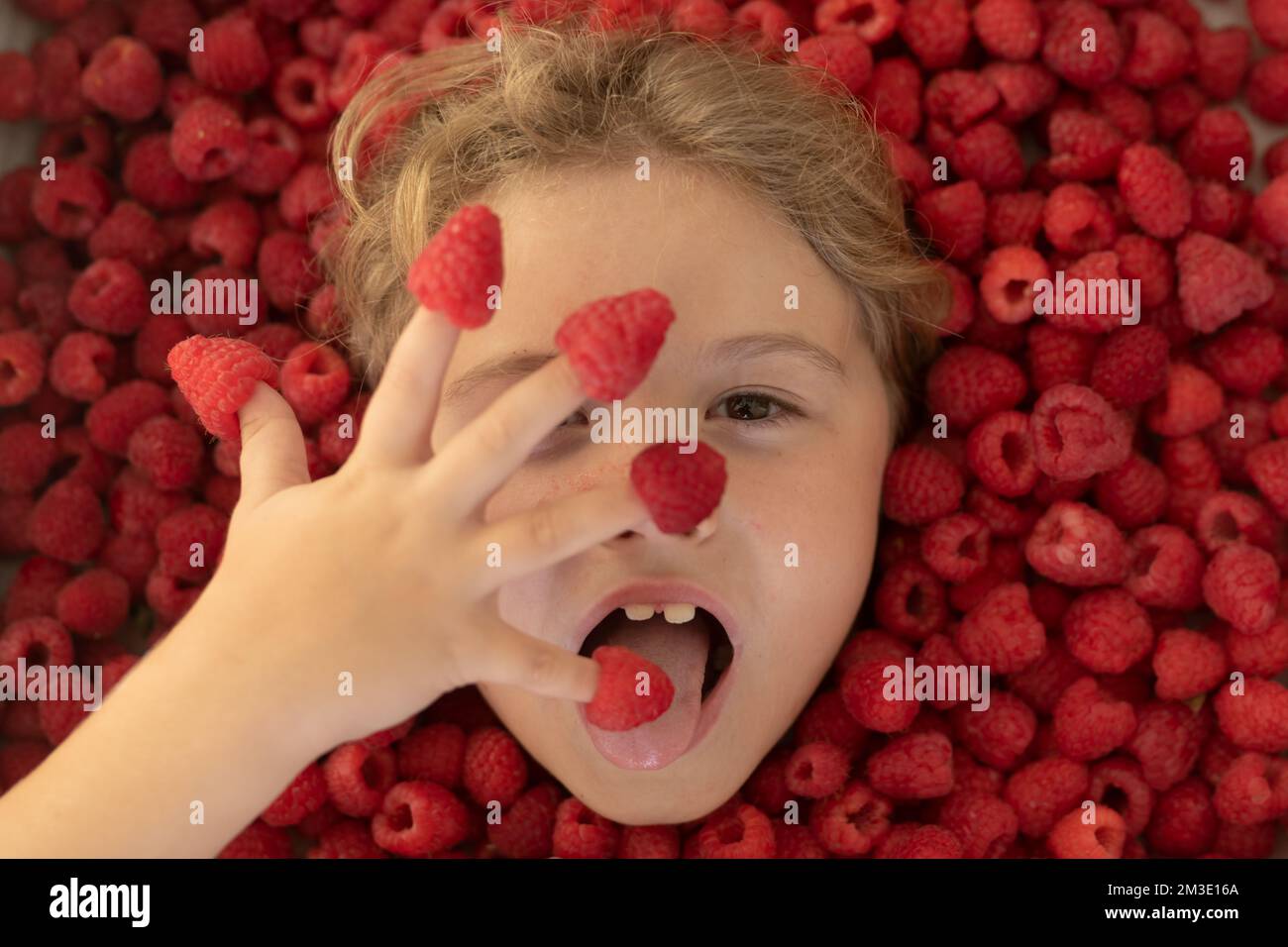 Kid eating raspberries. Top view photo of child face in raspberries ...