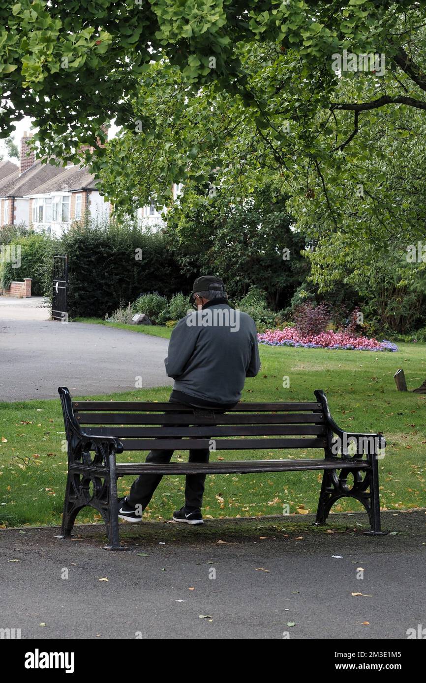 A vertical shot of a man leaning on a bench under a green tree in a ...