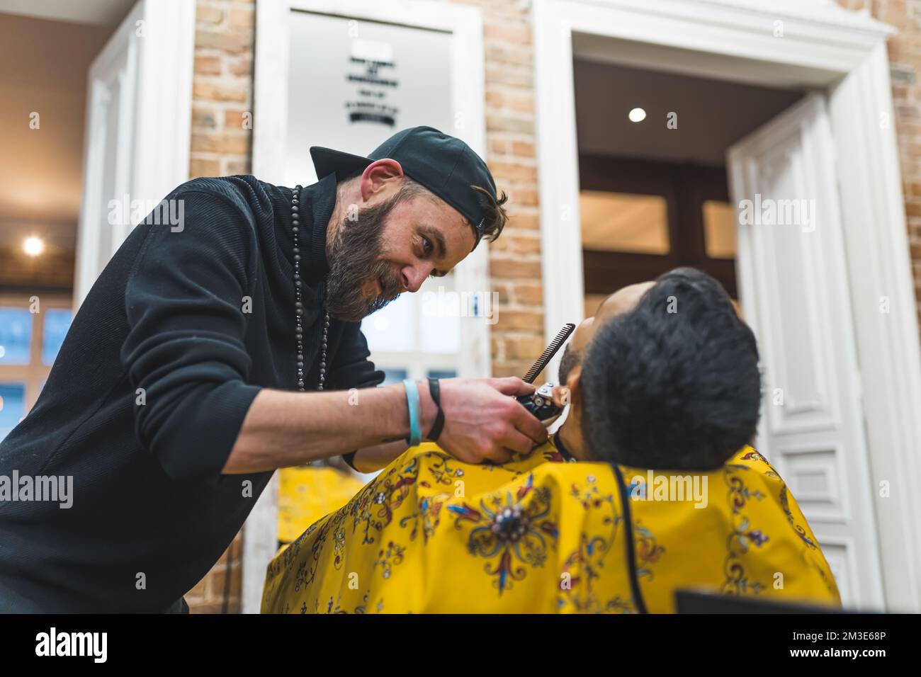 back view of a man getting beard haircut by a hairdresser at barbershop ...
