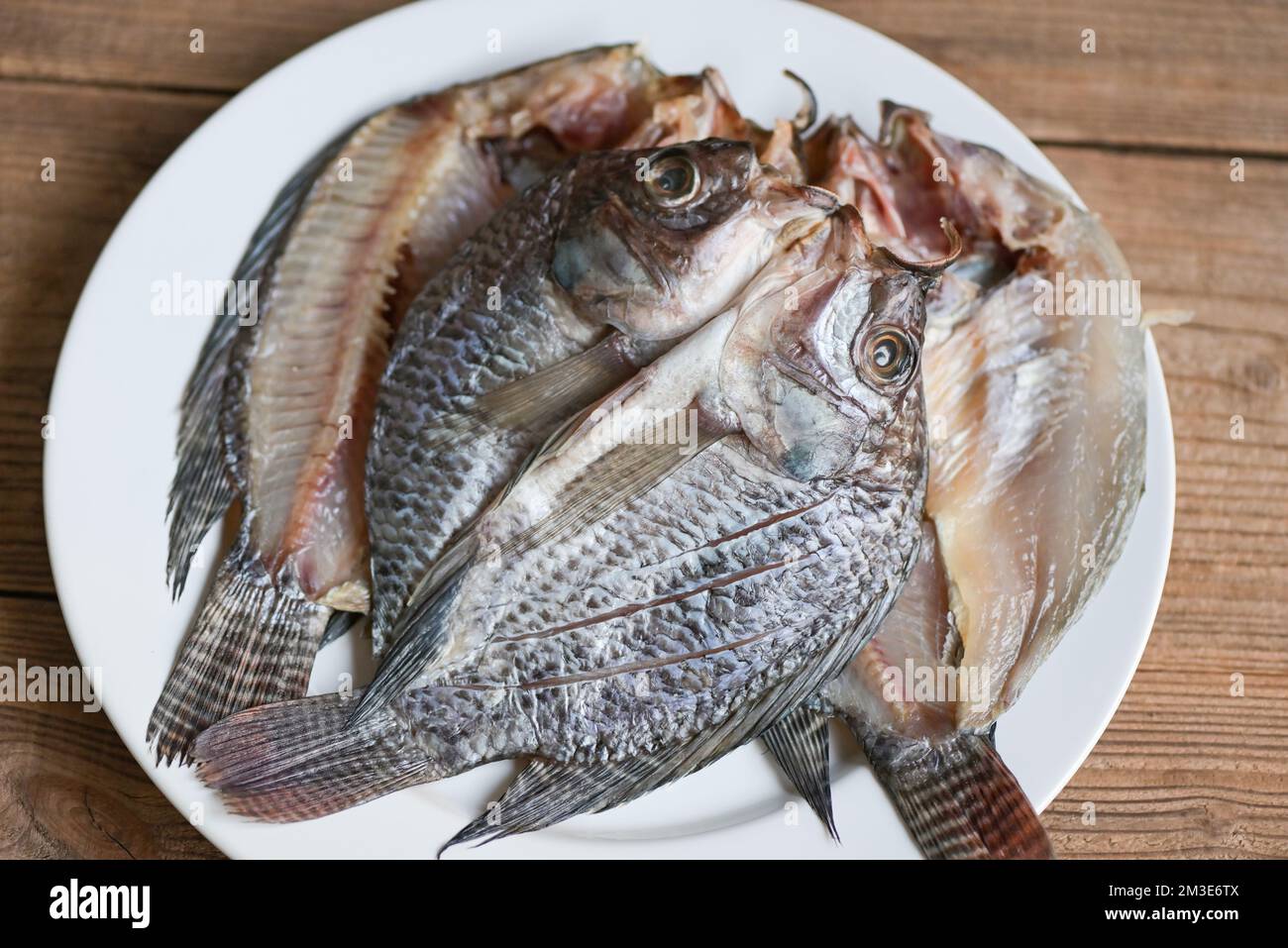dried fish on white plate, tilapia fish for cooking food on wooden ...