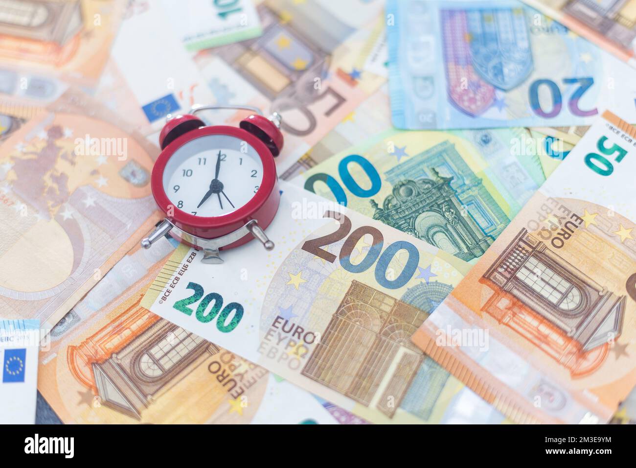 The clock stands on the euro banknotes, next to the coins. The concept ...