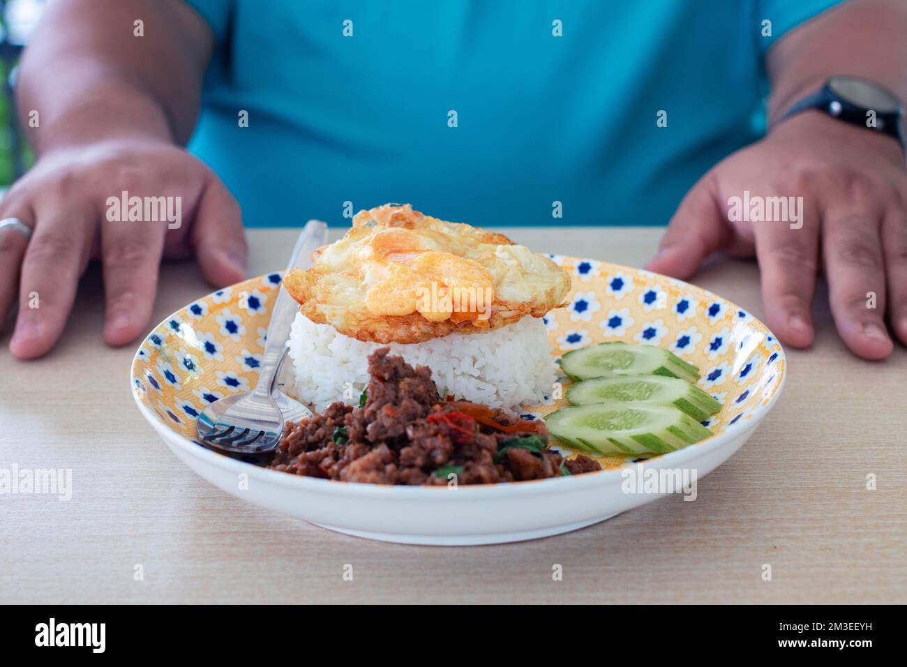 Pork basil rice with fried egg laying on the table with a fat man in ...