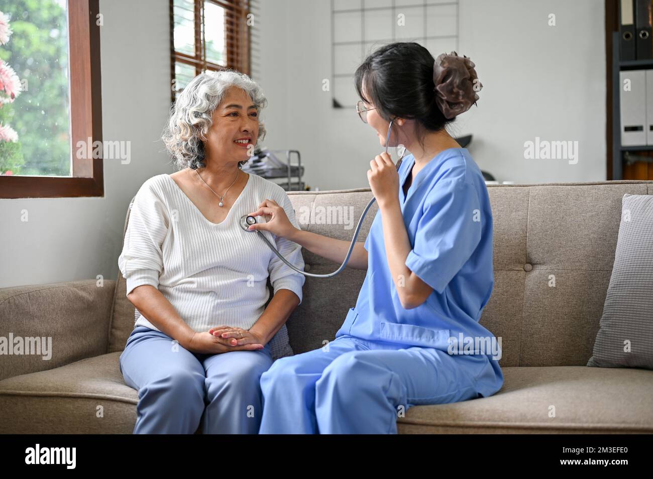 Professional Asian female doctor visiting her retire female patient at ...