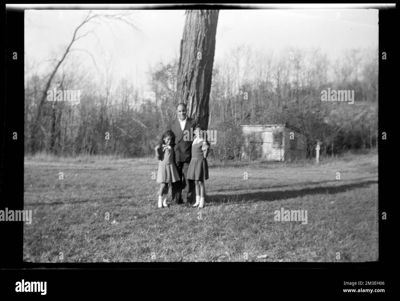 A man and two girls stand under a tree, shed in background , Girls ...