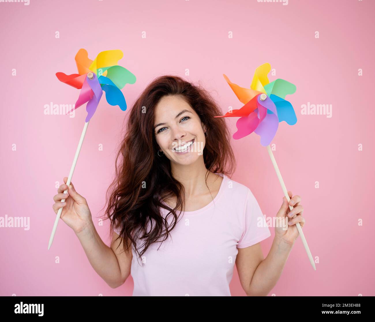 pretty young woman holding two colorful rainbow pinwheels and standing ...