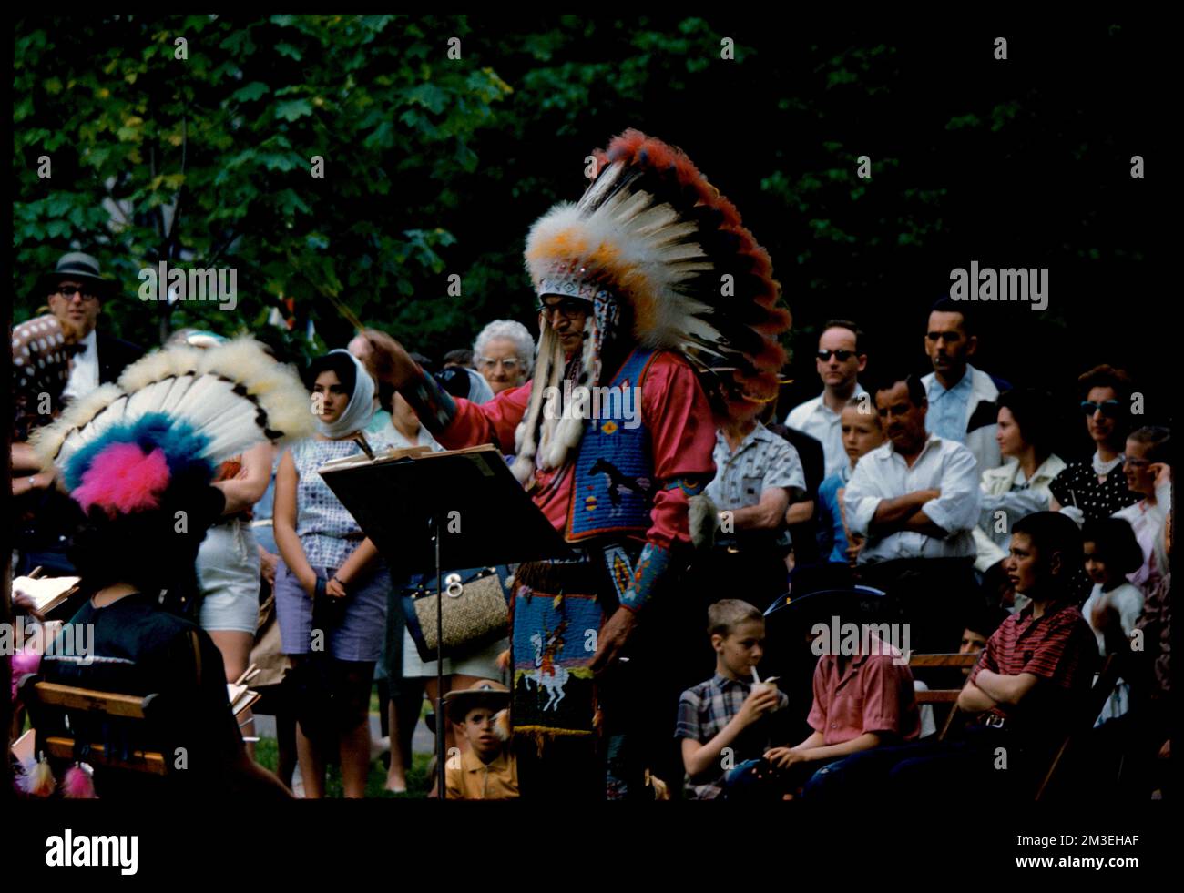 Man in feathered headdress conducting music while crowd watches ...