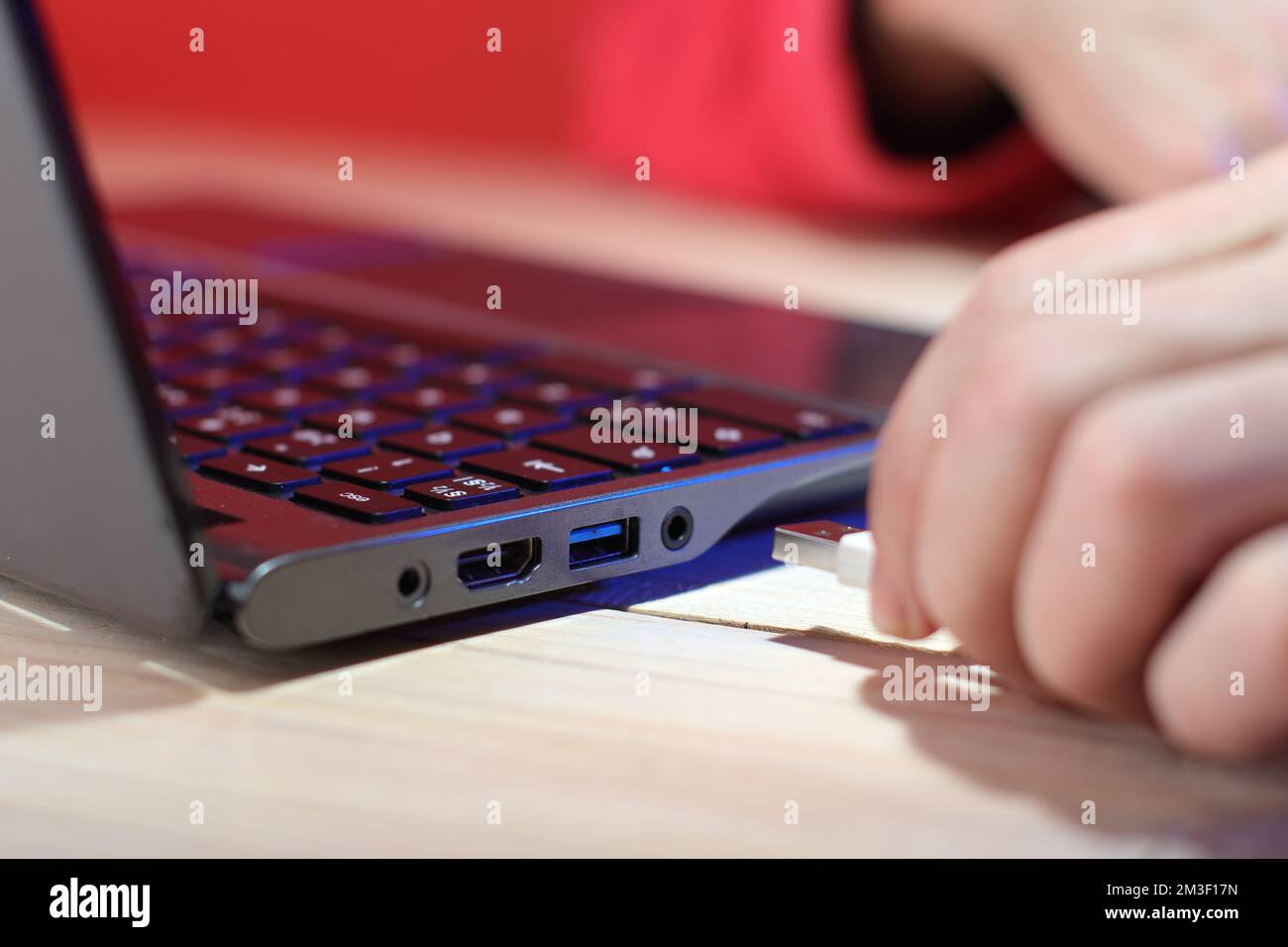 inserting a usb cable into a laptop on a table and colored background ...