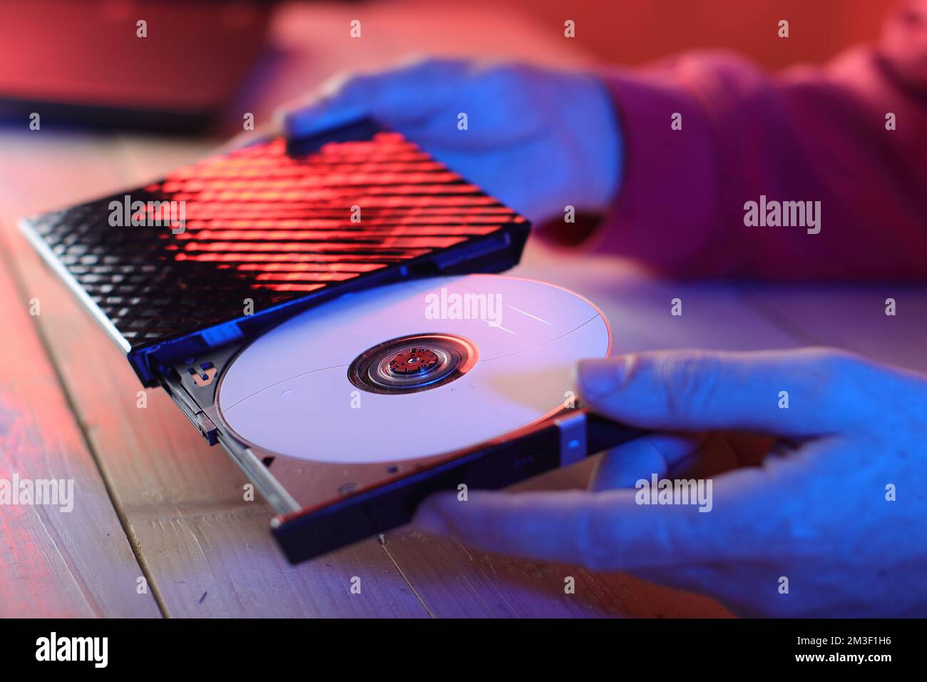 laptop optical drive with compact disc in hands on table and colored ...