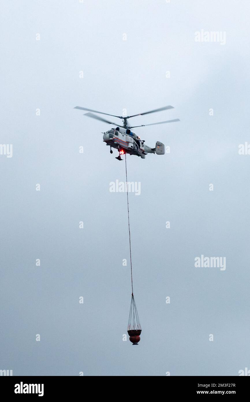 A fire helicopter carries a container of water to extinguish a fire in ...