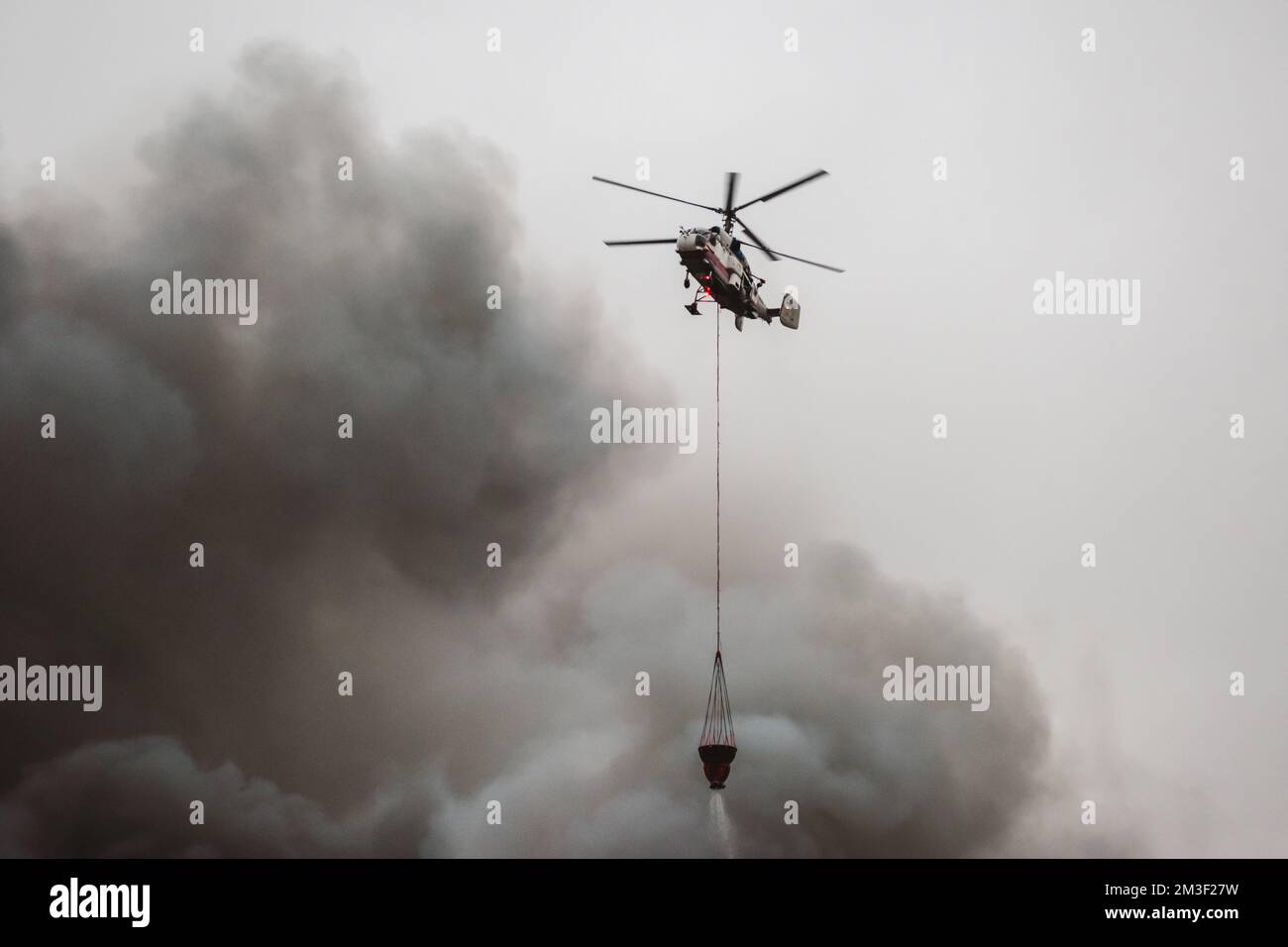 A fire helicopter carries a container of water to extinguish a fire in ...