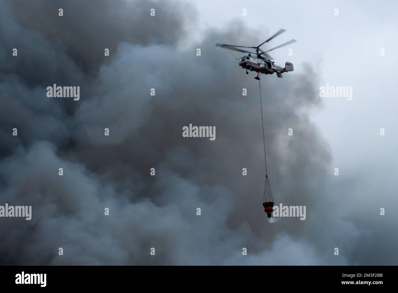 A fire helicopter carries a container of water to extinguish a fire in ...