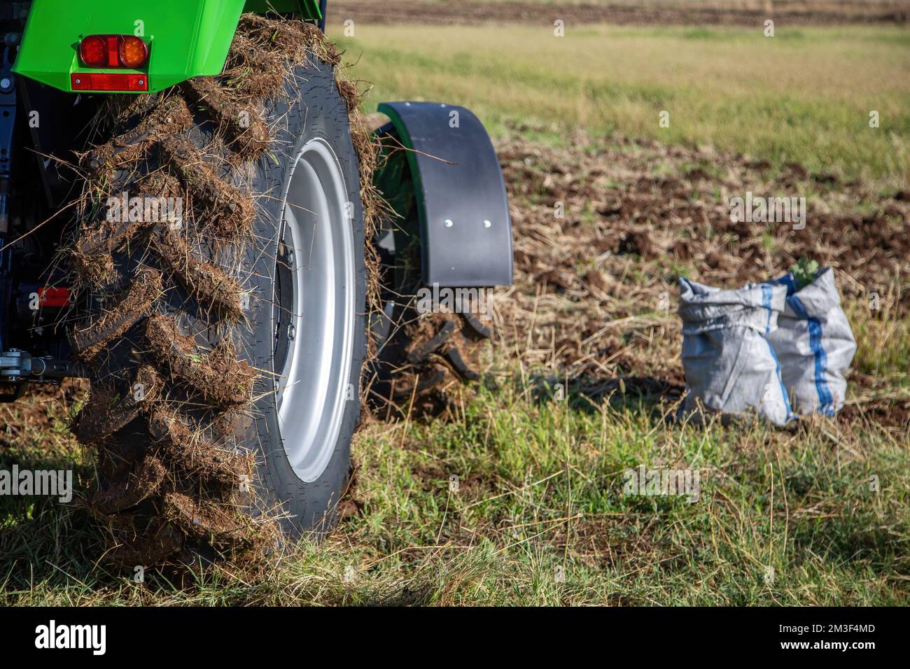 Agriculture concept. Tractor wheel covered with mud, sack with seed ...