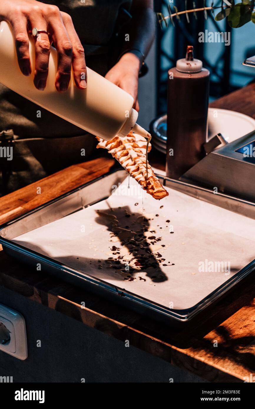 A cook making a waffle with sweet topping in a restaurant, a vertical ...