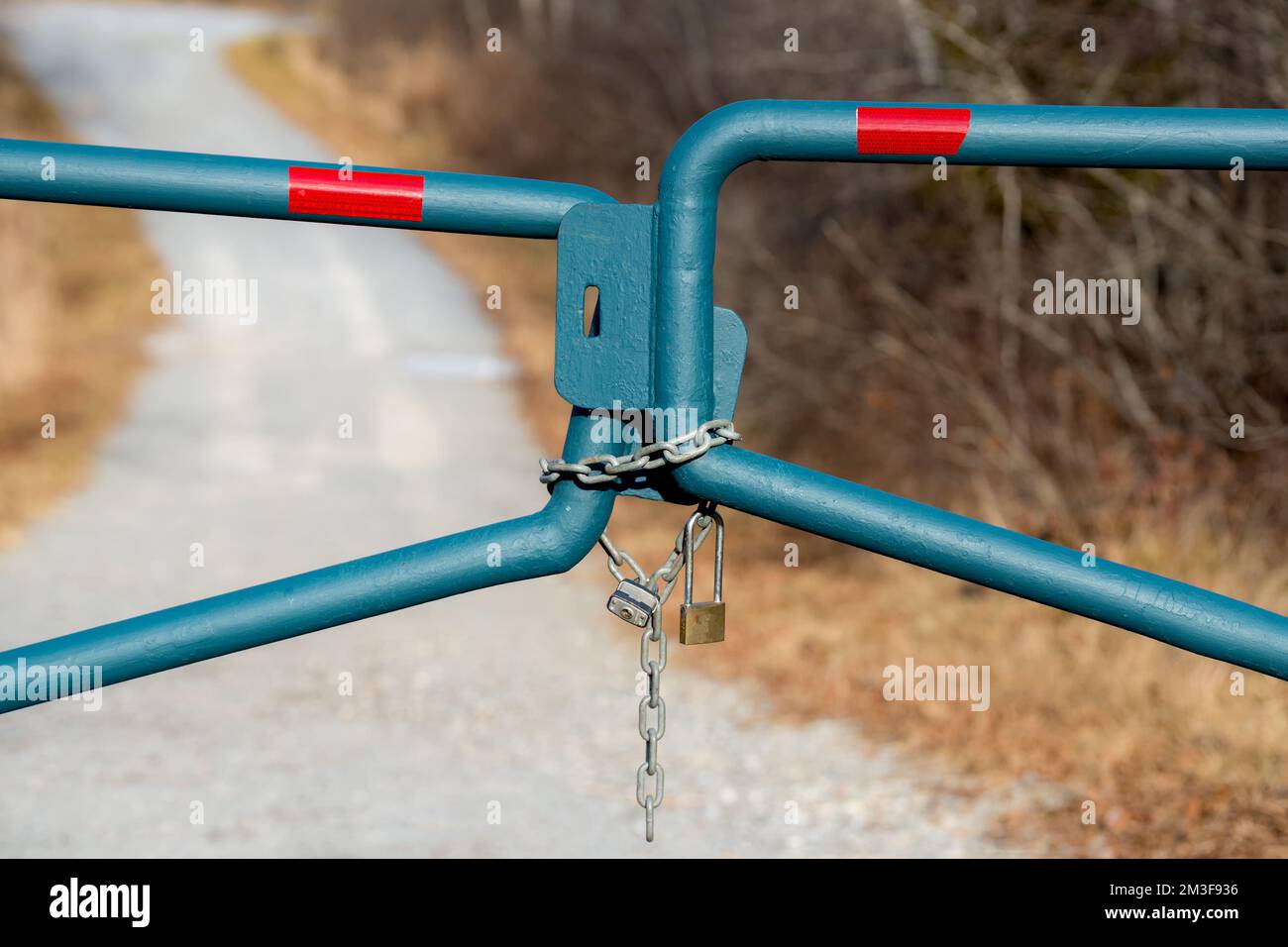 Locked gate blocking a gravel road. Two padlocks visible. Red ...