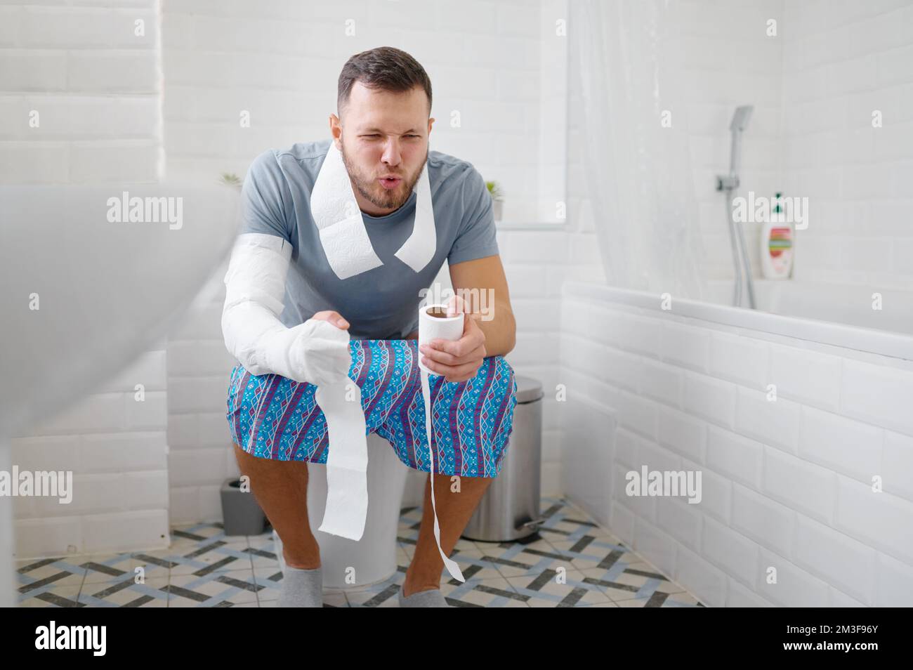 Frowning displeased young adult man sitting on toilet suffers from ...