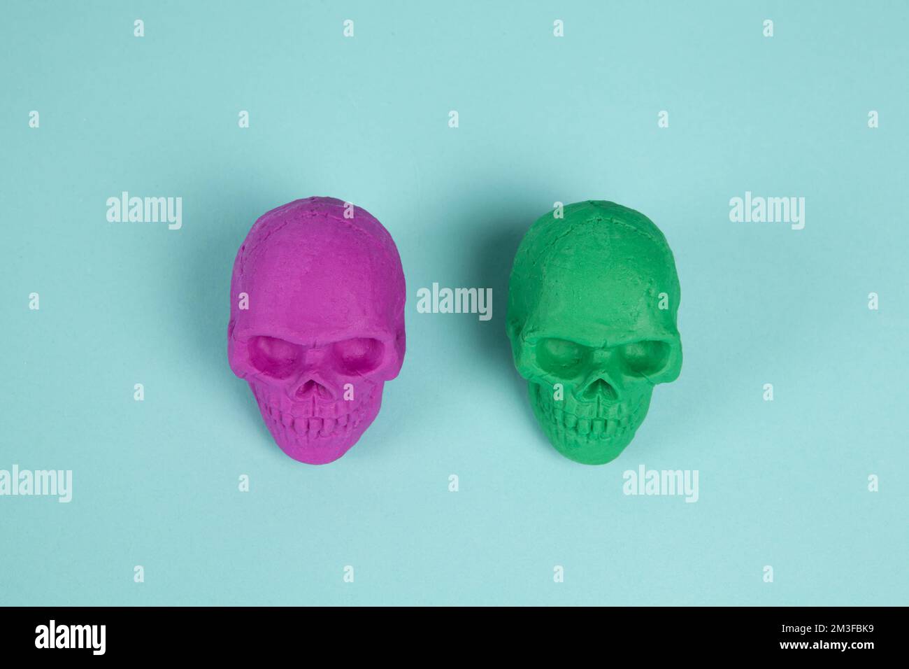 Two plastic skulls, one pink and one green, placed on a turquoise ...