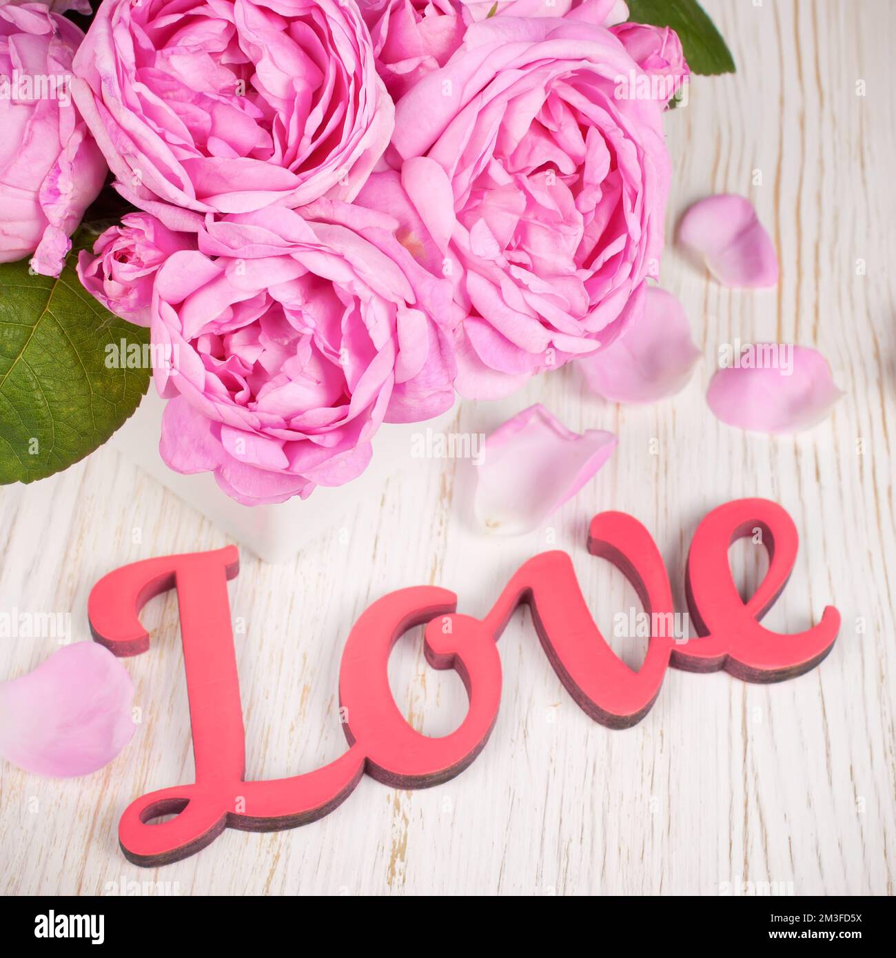 Pink roses and petals on wooden white desk and red wooden word love ...