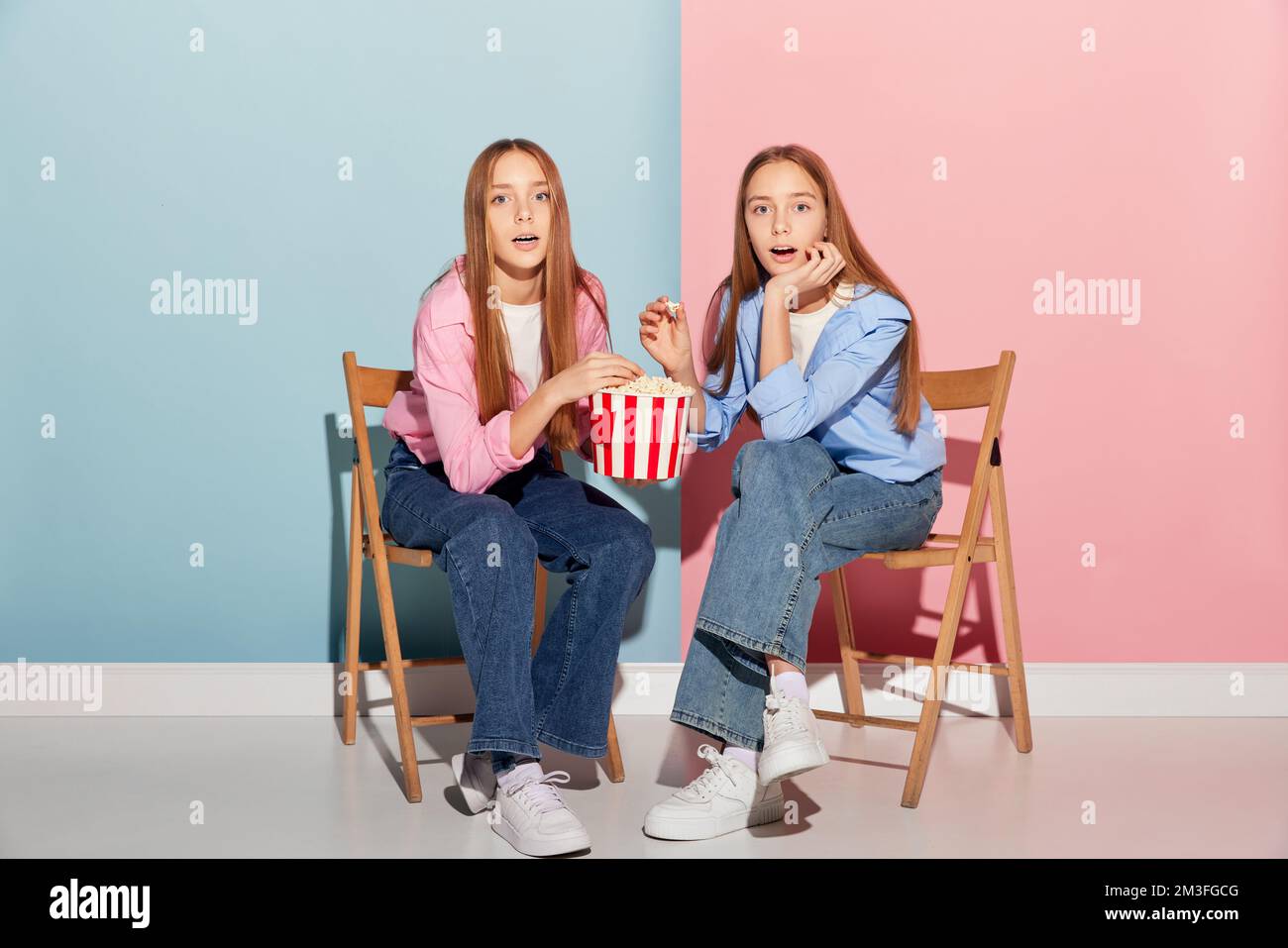 Two cheerful funky girls sitting watching movie and eating popcorn ...