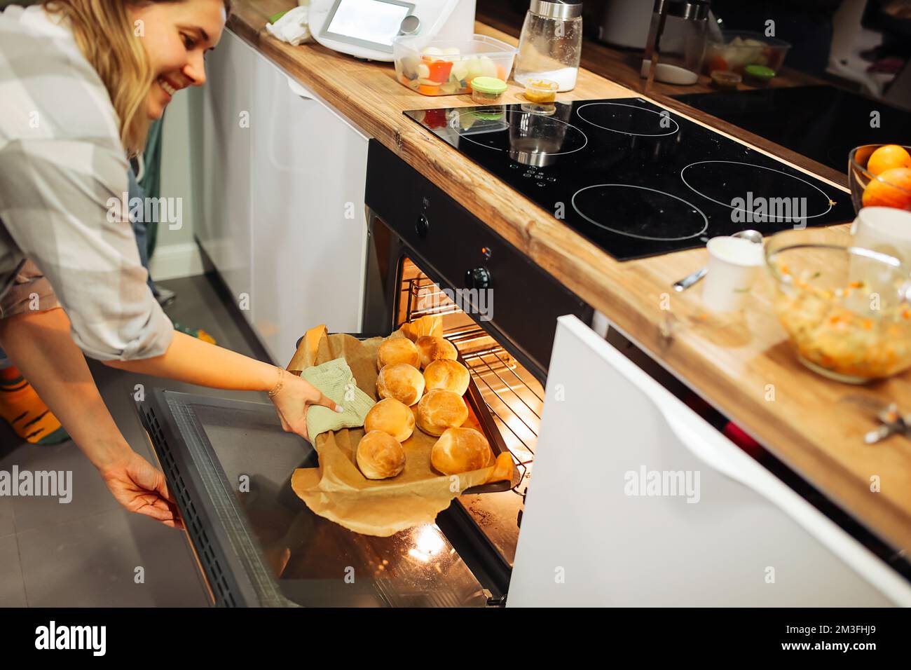 Cropped laughing blond woman pulling tray of buns on baking paper out ...