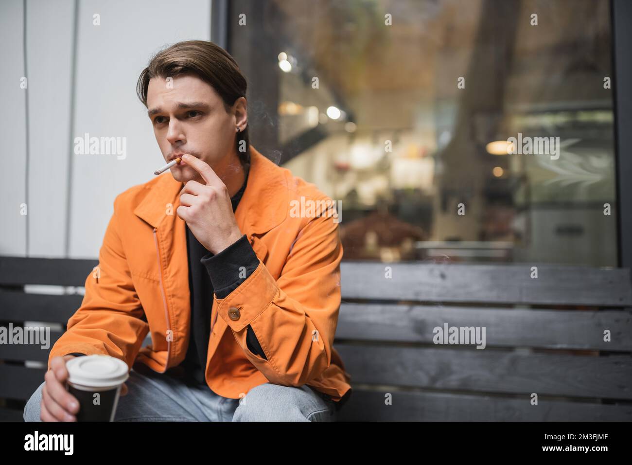 Stylish man smoking cigarette and holding coffee to go near cafe,stock ...