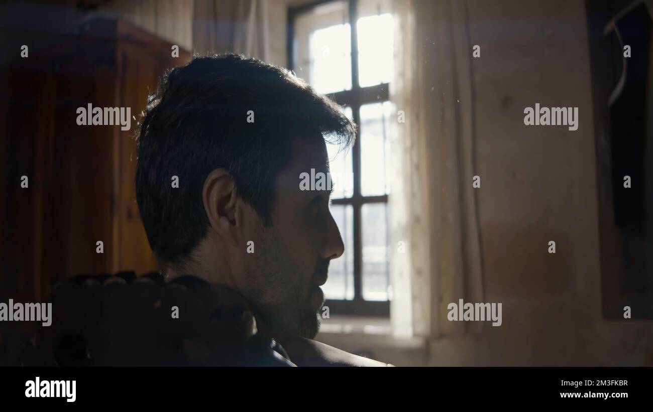 Man with black hair sitting in old room interior in front of a window ...