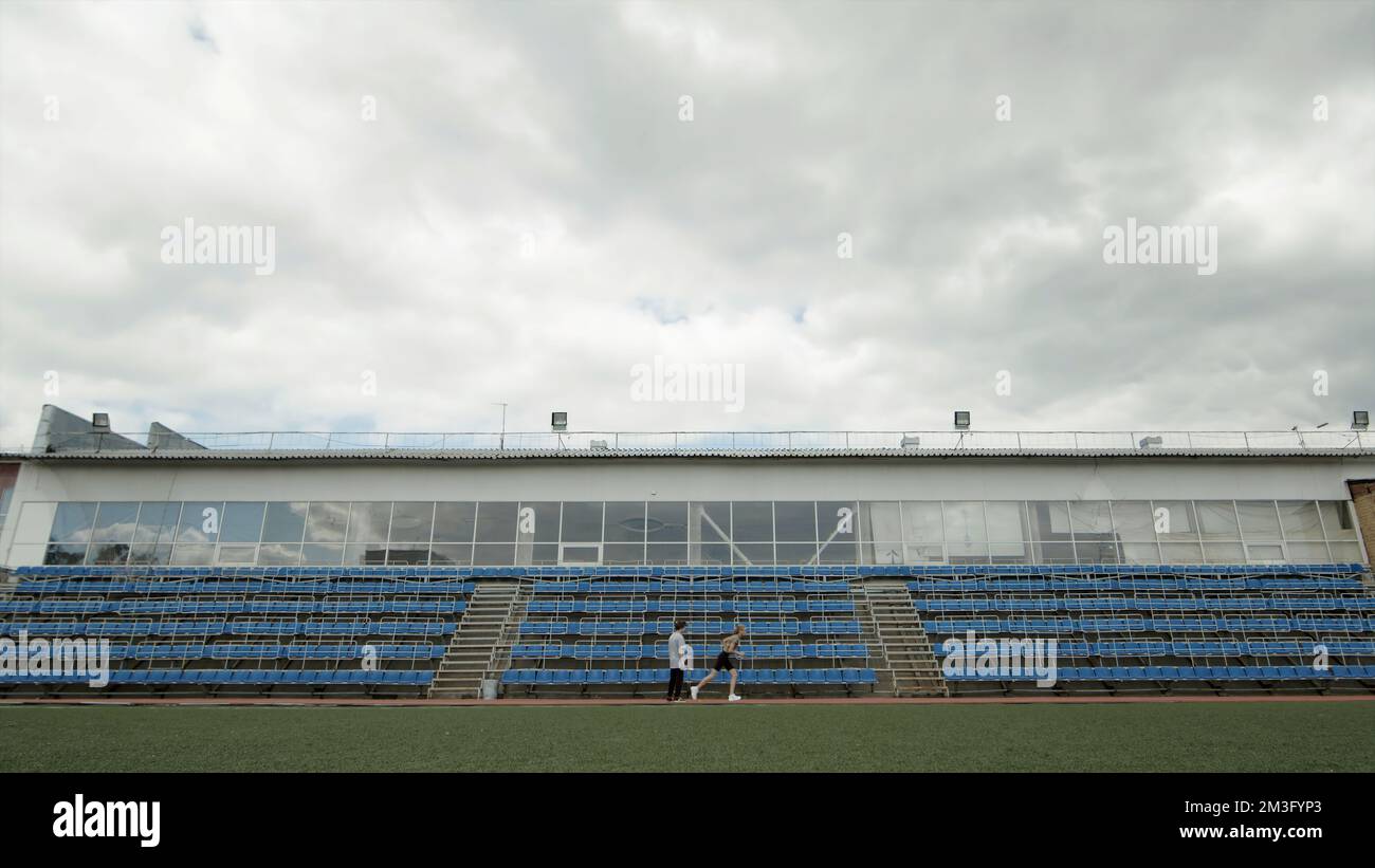 Sports field with training athletes with empty seats and cloudy sky on ...