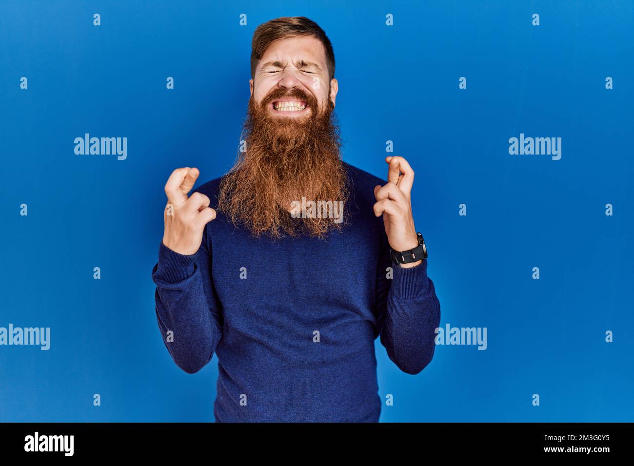 Redhead man with long beard wearing casual blue sweater over blue ...
