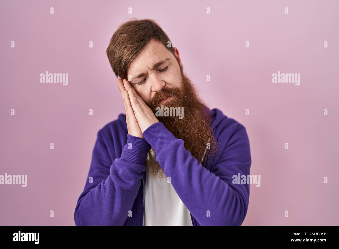 Caucasian man with long beard standing over pink background sleeping ...
