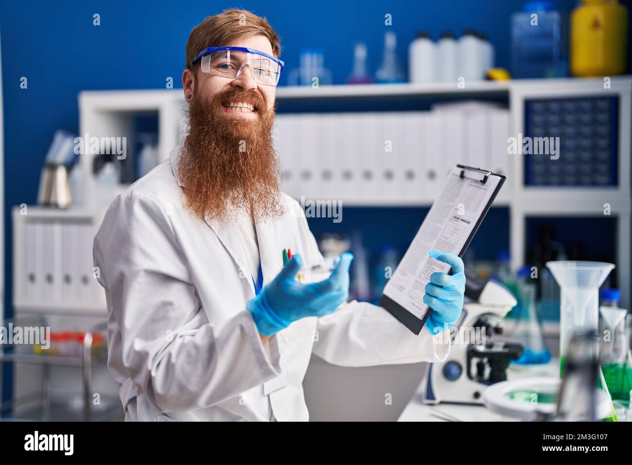 Young redhead man scientist reading report holding sample at laboratory ...