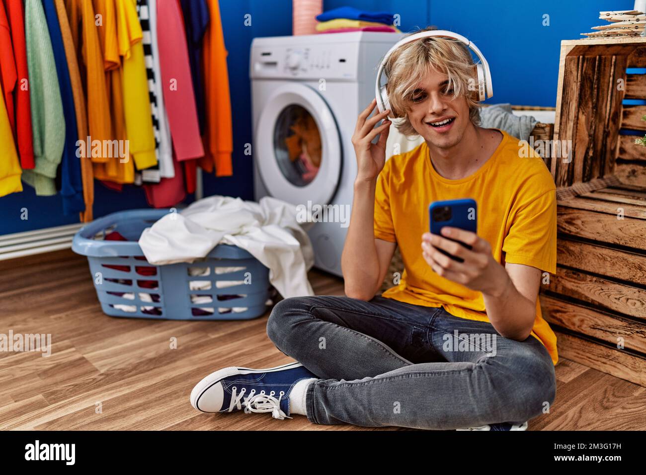 Young blond man listening to music waiting for washing machine at ...