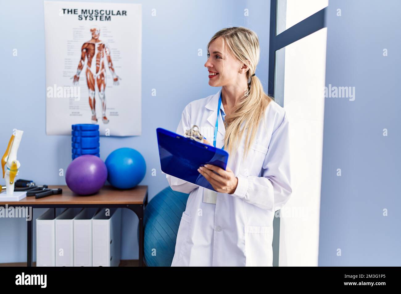 Young blonde woman wearing physiotherpist uniform writing on checklist ...