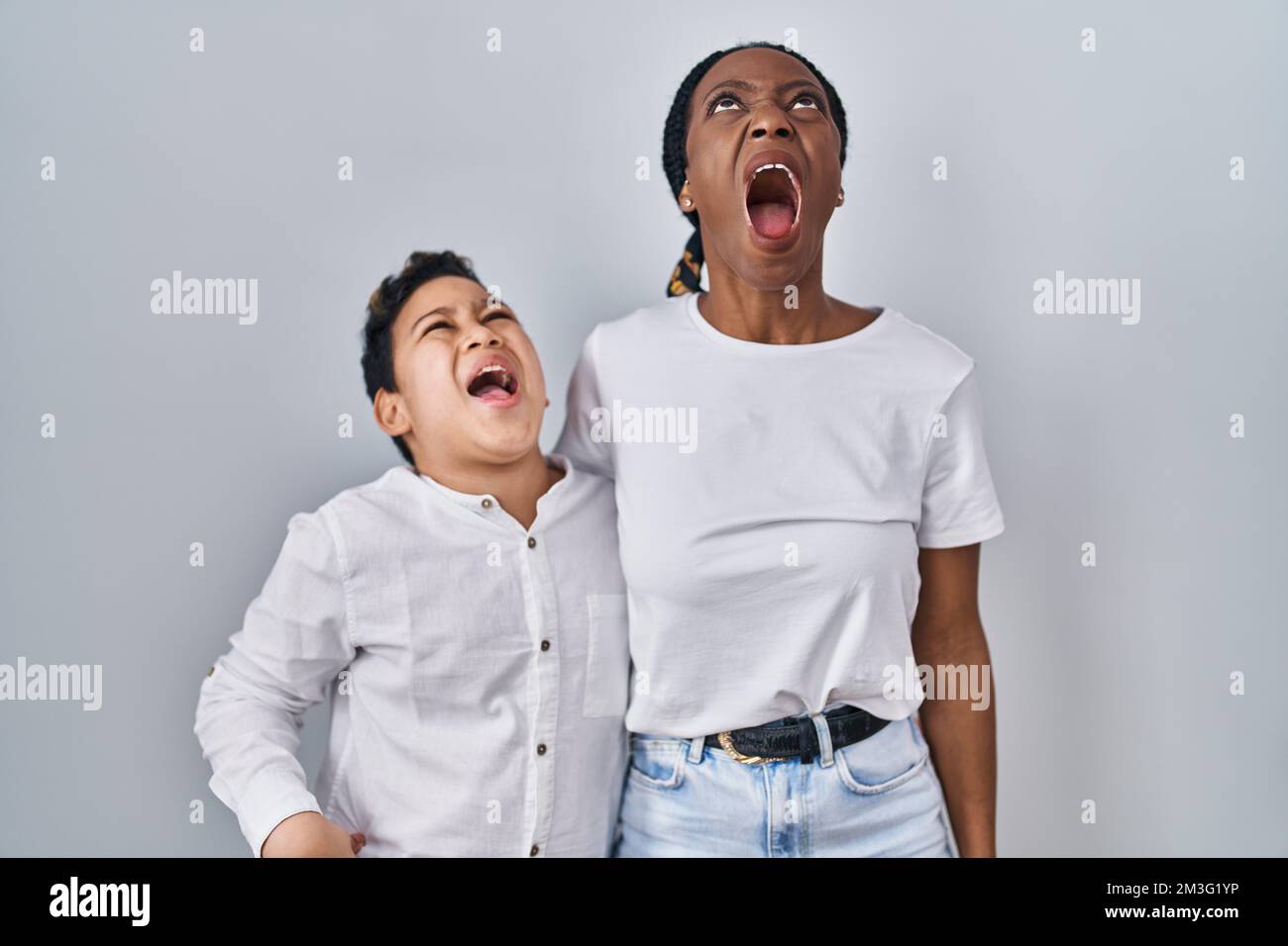 Young mother and son standing together over white background angry and ...
