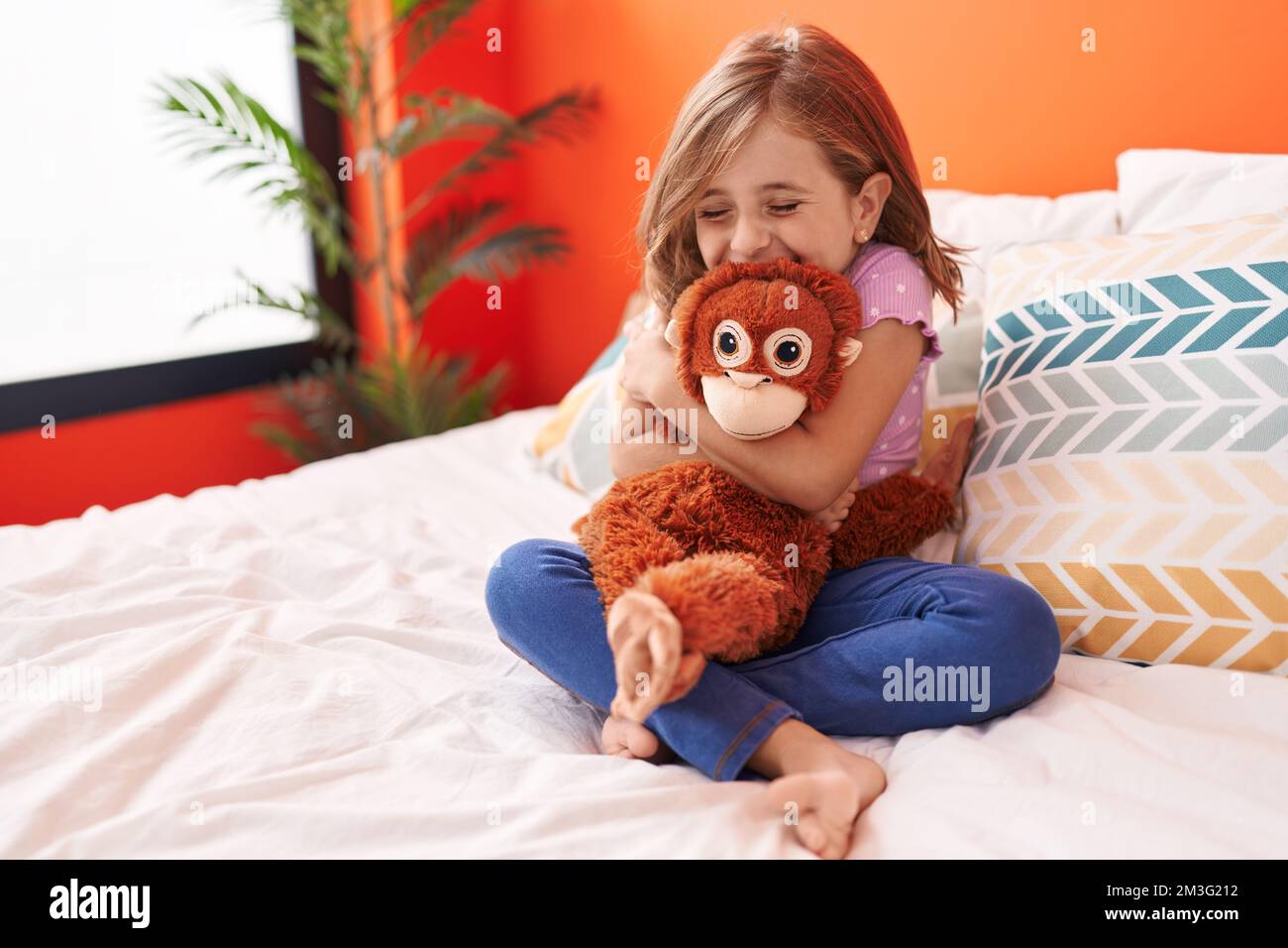 Adorable hispanic girl hugging monkey doll sitting on bed at bedroom ...
