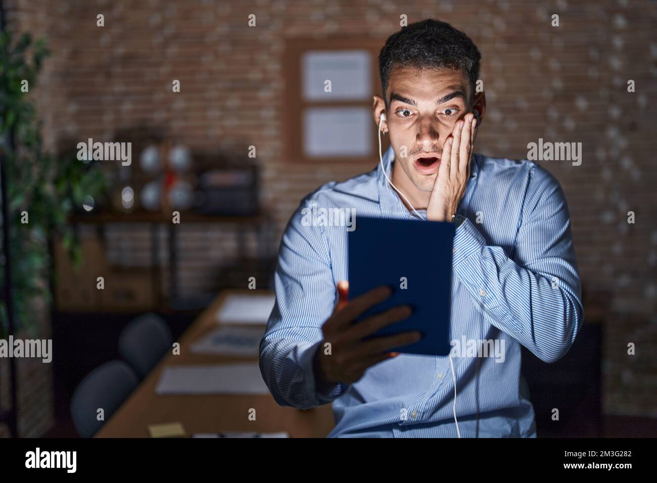 Handsome hispanic man working at the office at night afraid and shocked ...