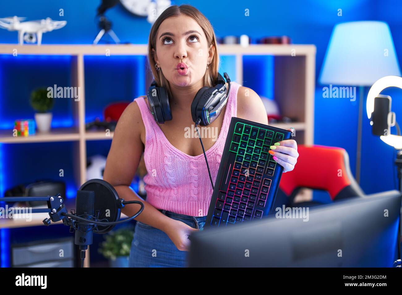 Young blonde woman playing video games holding keyboard making fish ...