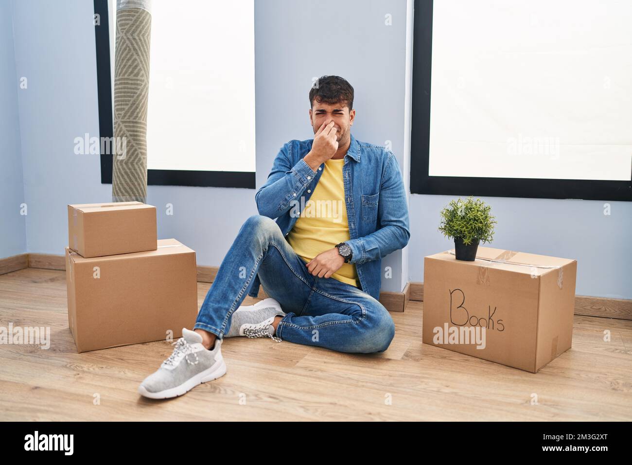 Young hispanic man sitting on the floor at new home smelling something ...