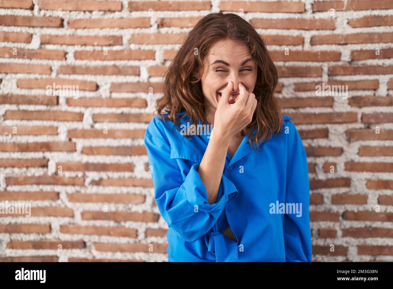 Beautiful brunette woman standing over bricks wall smelling something ...
