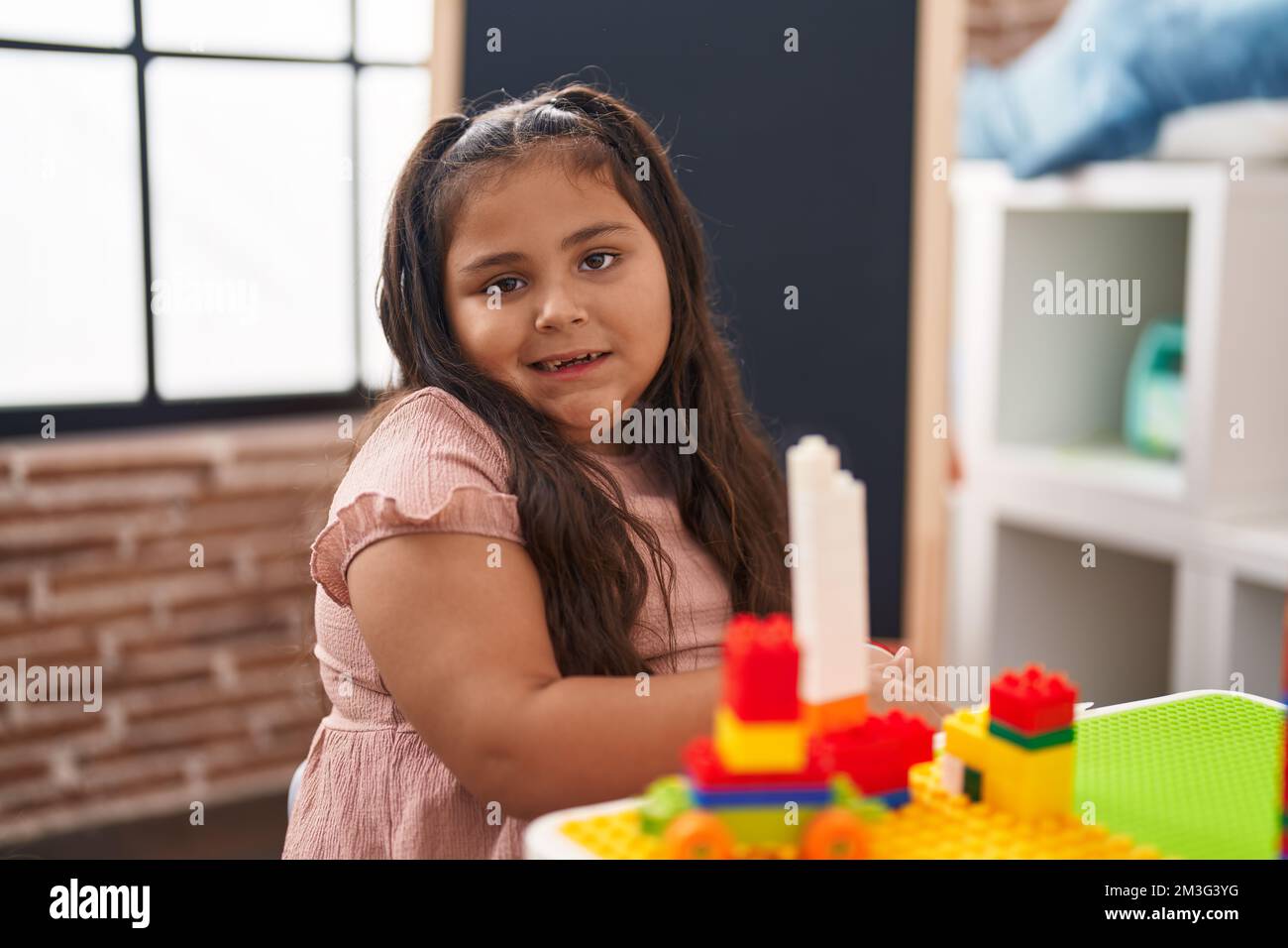 Plus size hispanic girl playing with construction blocks sitting on table at kindergarten Stock ...