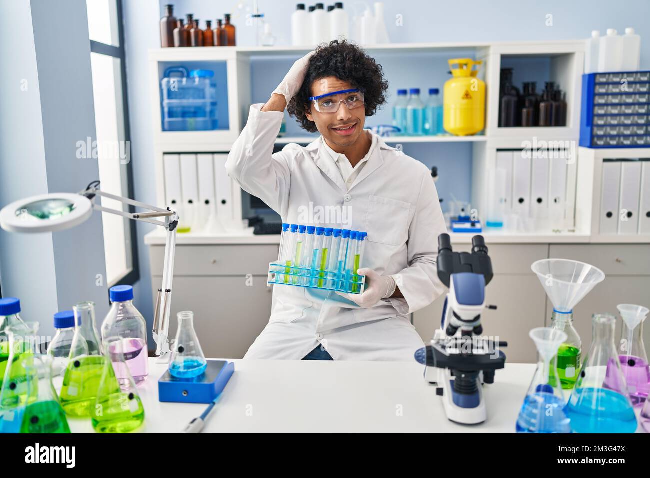 Hispanic man with curly hair working at scientist laboratory stressed ...