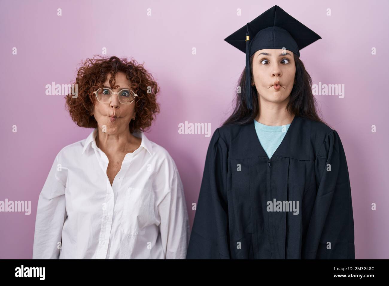 Hispanic mother and daughter wearing graduation cap and ceremony robe ...