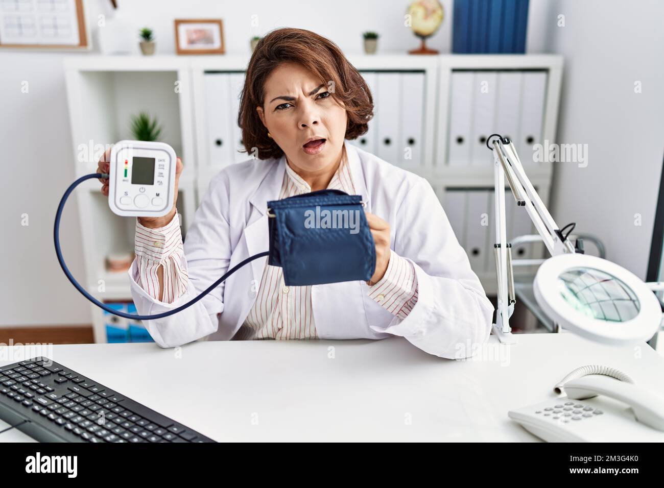 Middle age hispanic doctor woman using blood pressure monitor in shock ...
