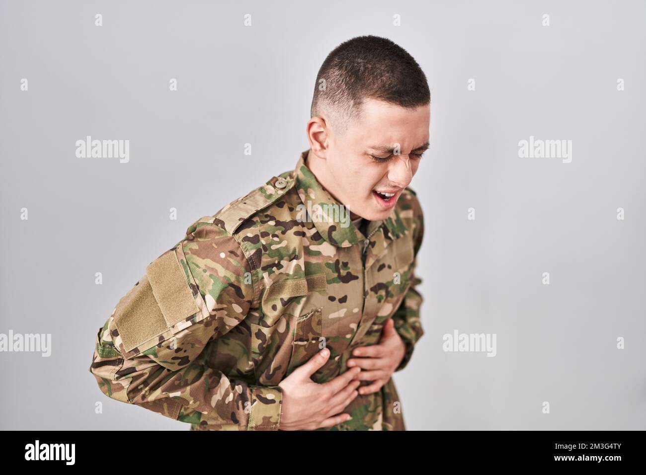 Young man wearing camouflage army uniform with hand on stomach because ...