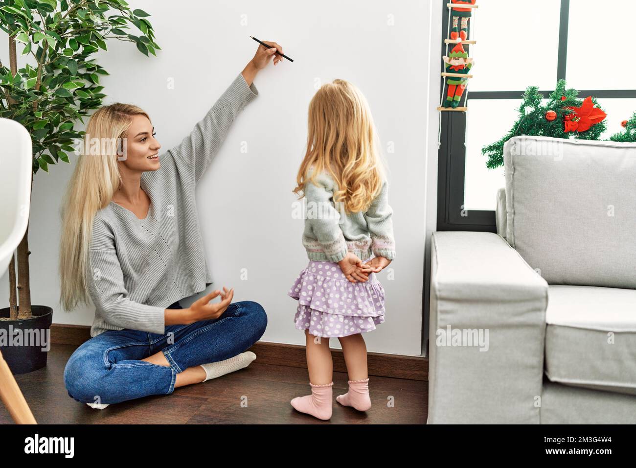 Mother and daughter measuring child height writing mark on wall at home ...