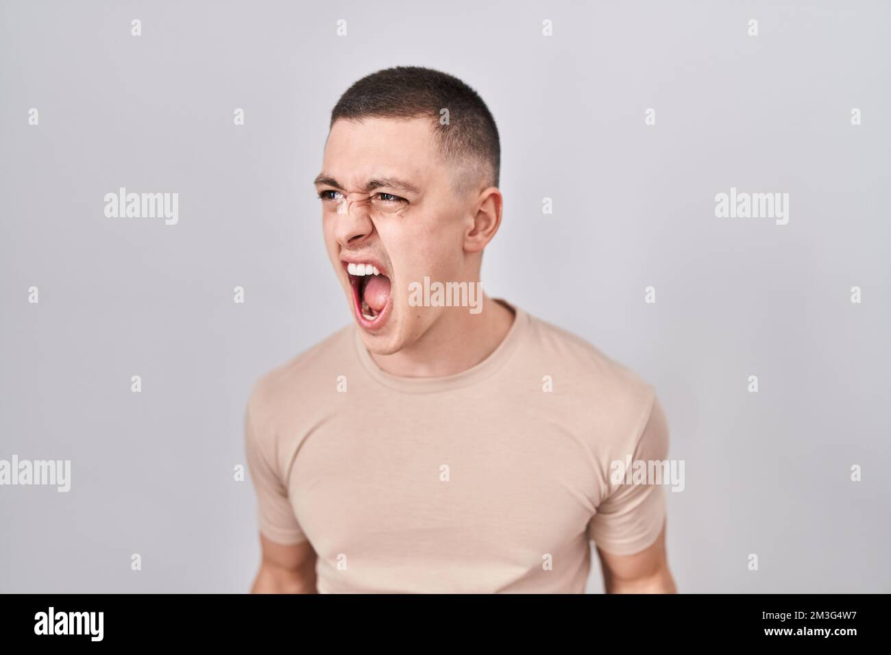 Young man standing over isolated background angry and mad screaming ...
