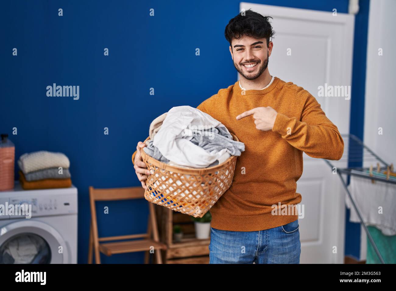 Hispanic man with beard holding laundry basket at laundry room smiling ...