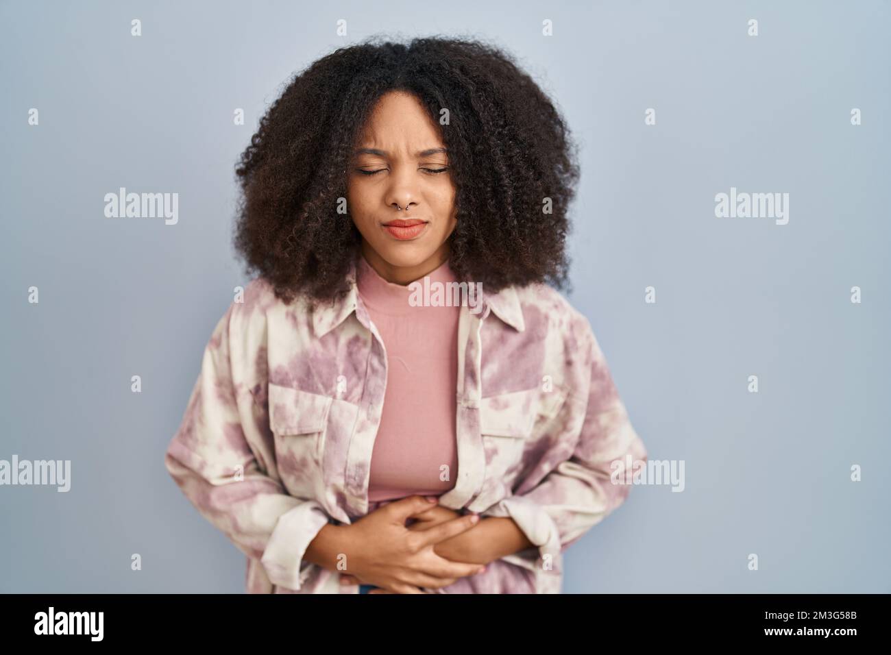 Young african american woman standing over blue background with hand on ...