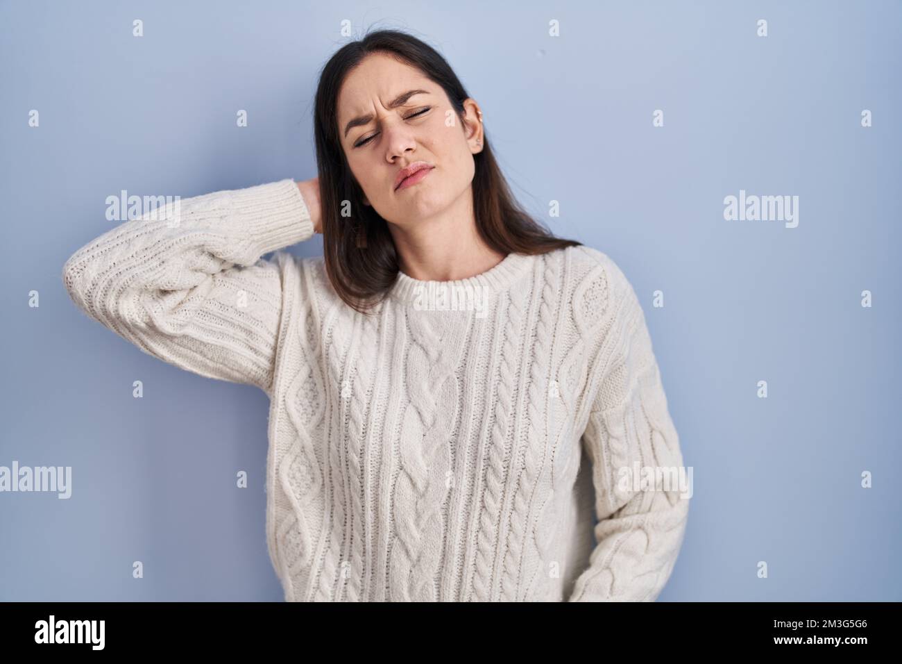 Young brunette woman standing over blue background suffering of neck ...