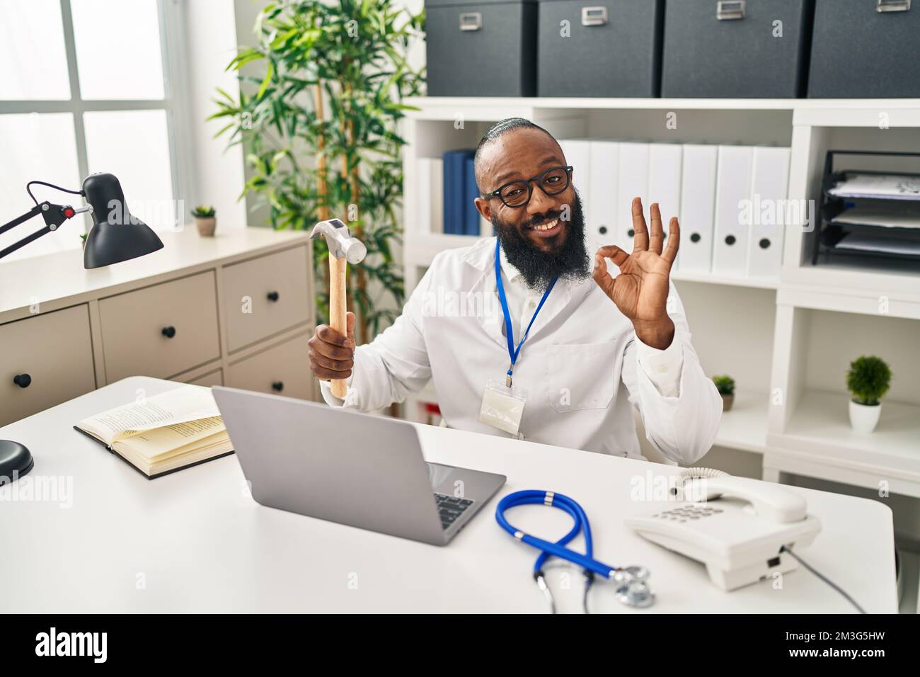 African american man working at medical clinic holding hammer doing ok ...