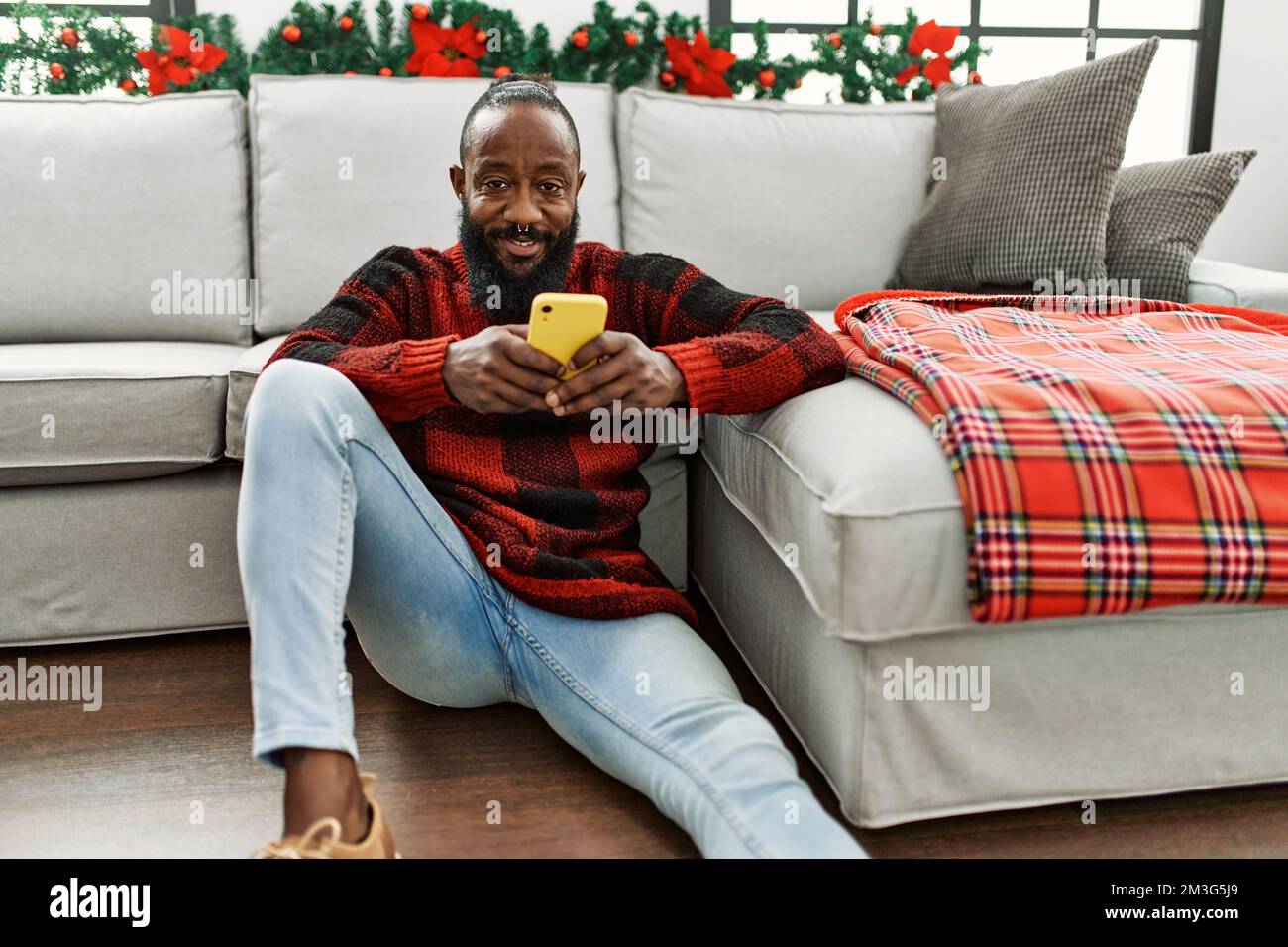 Young african american man using smartphone sitting by christmas decor ...
